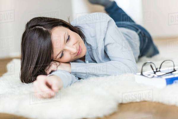 Mid adult woman lying on fur rug - Stock Photo - Dissolve
