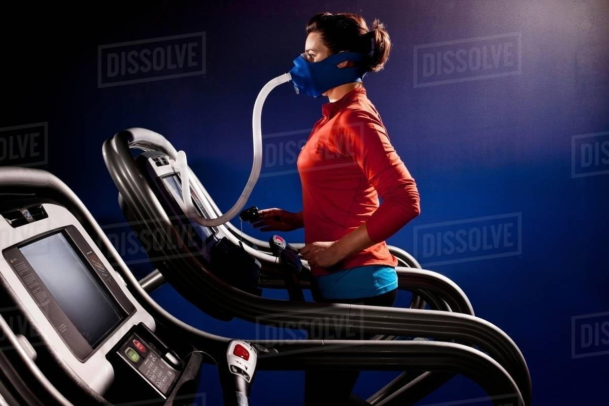 Mid adult woman with face mask running on gym treadmill in altitude ...