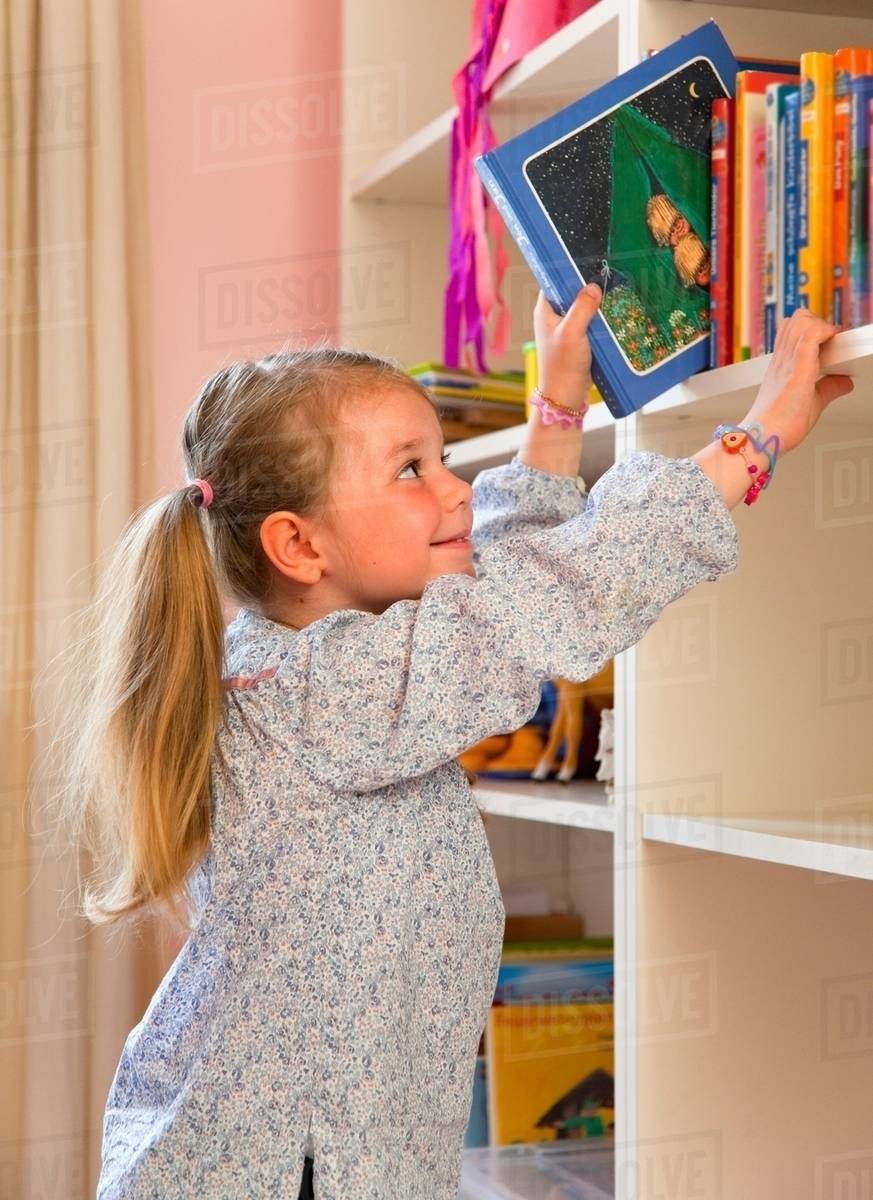 Girl pulling books from bookshelf - Royalty-free Stock Photo | Dissolve