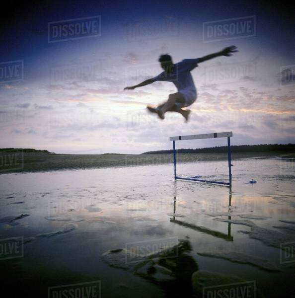 Man jumping hurdle in water on beach - Stock Photo - Dissolve