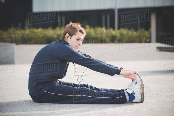 Young man touching toes in city square - Stock Photo - Dissolve