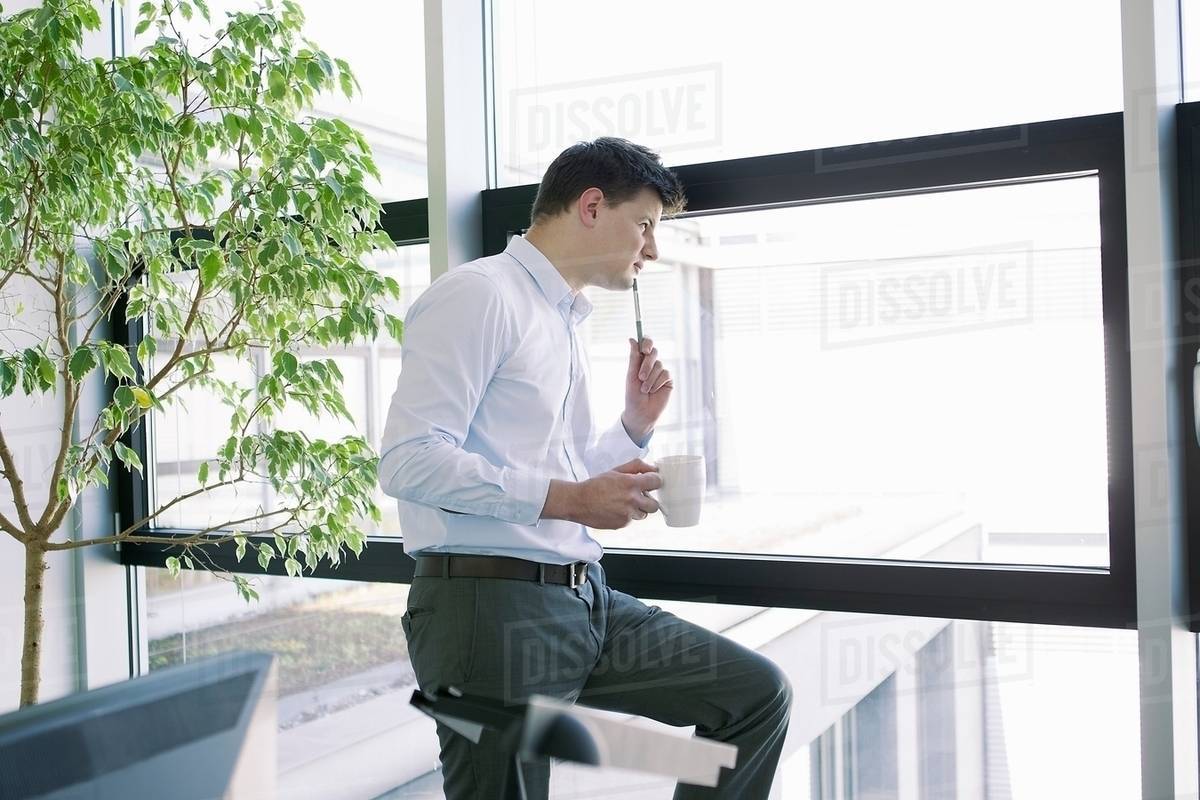 Businessman peering out office window - Royalty-free Stock Photo | Dissolve