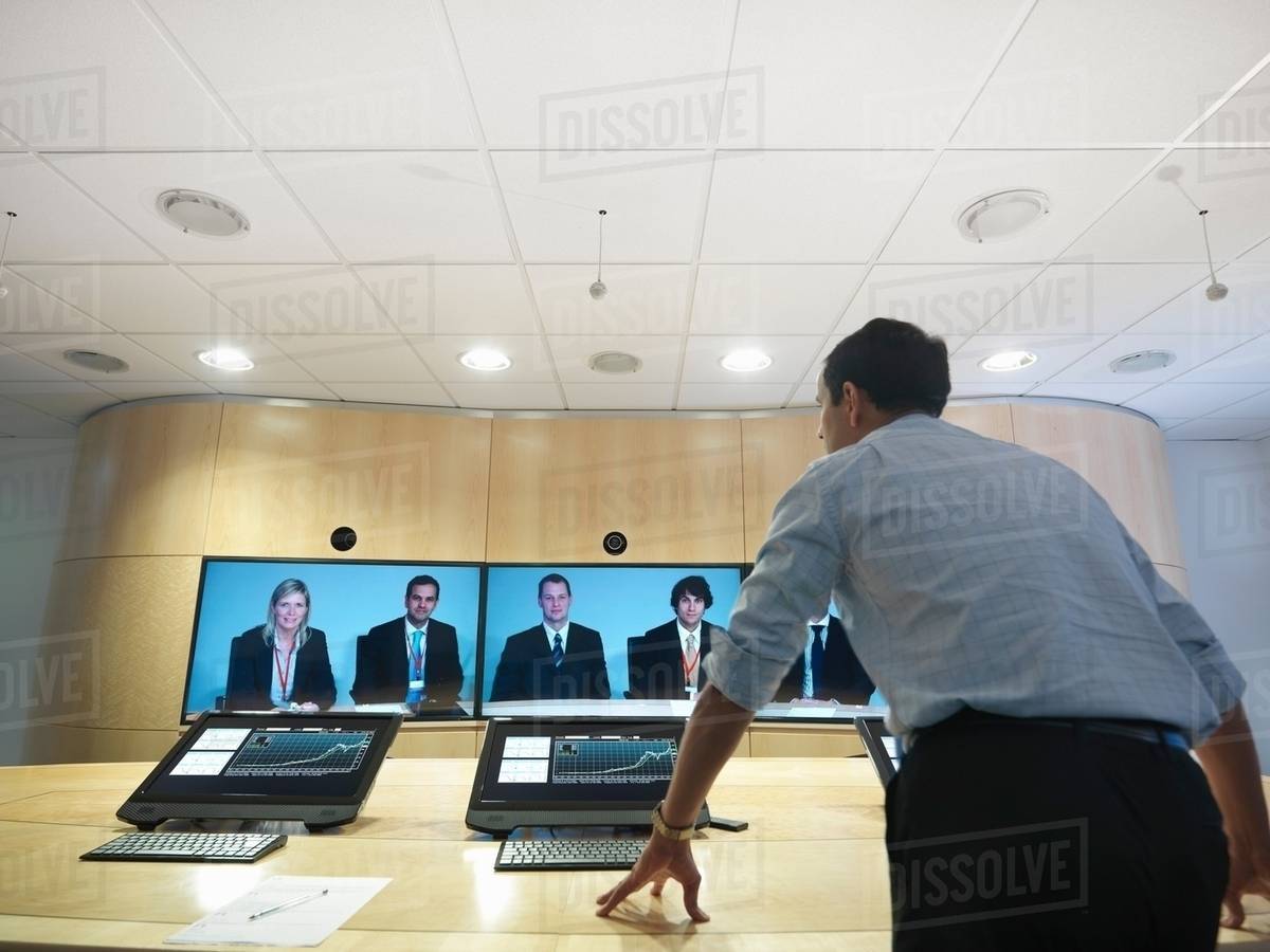Businessman standing in meeting room addressing colleagues on video ...
