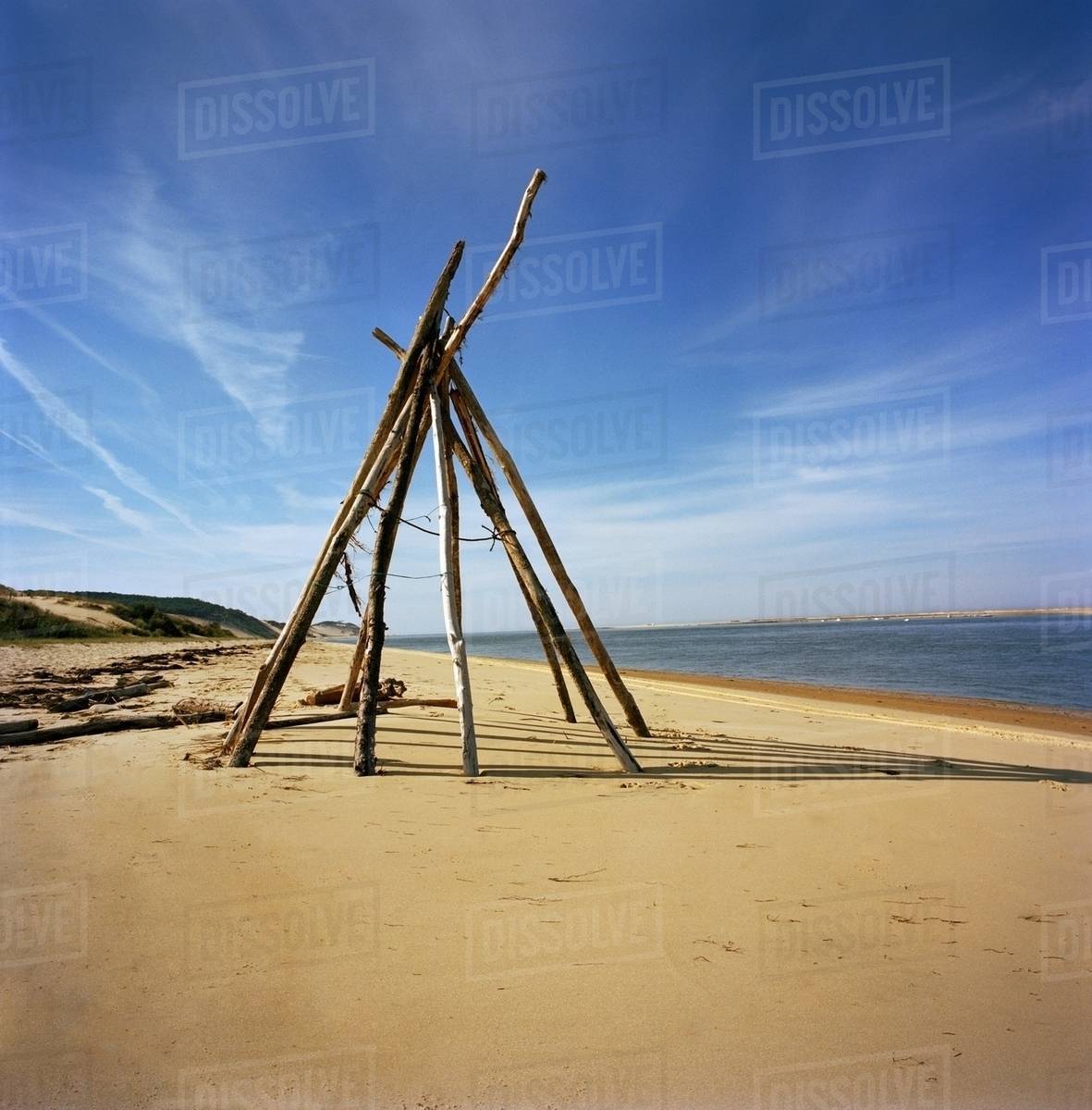 Log teepee on sandy beach - Stock Photo - Dissolve