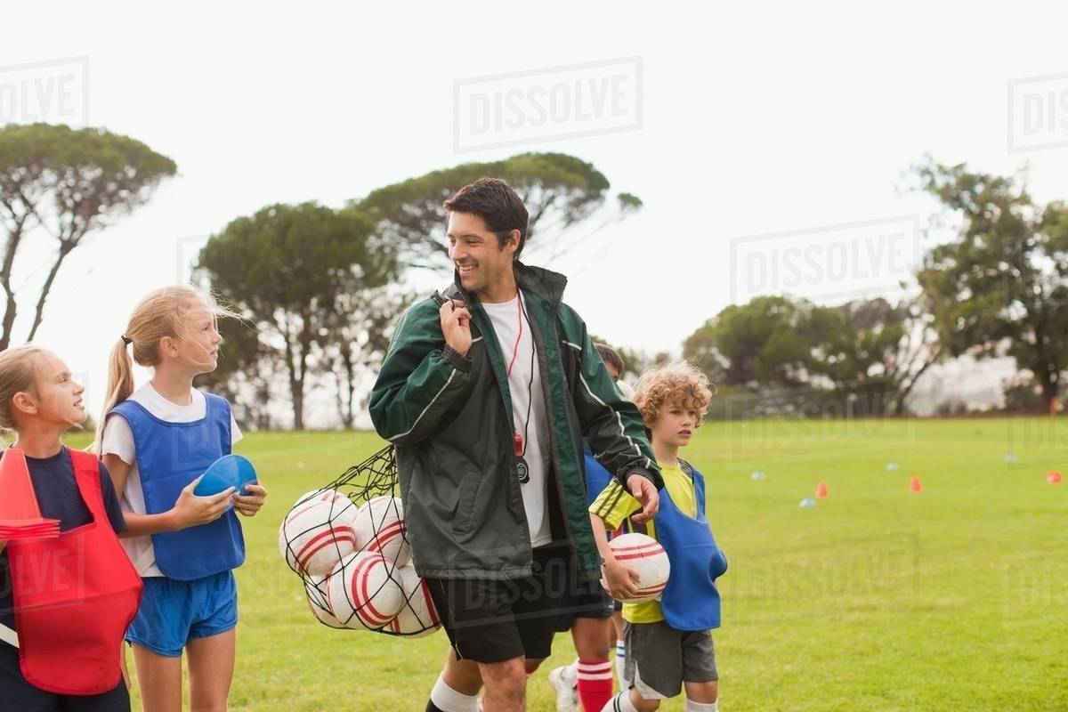 Coach carrying soccer balls on pitch - Royalty-free Stock Photo | Dissolve