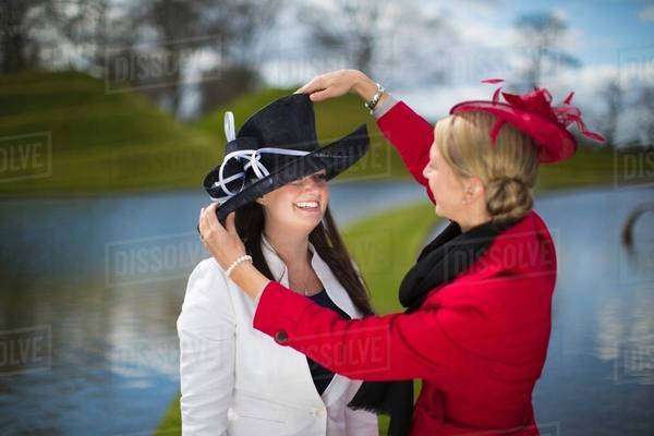 Women adjusting decorative hats - Stock Photo - Dissolve