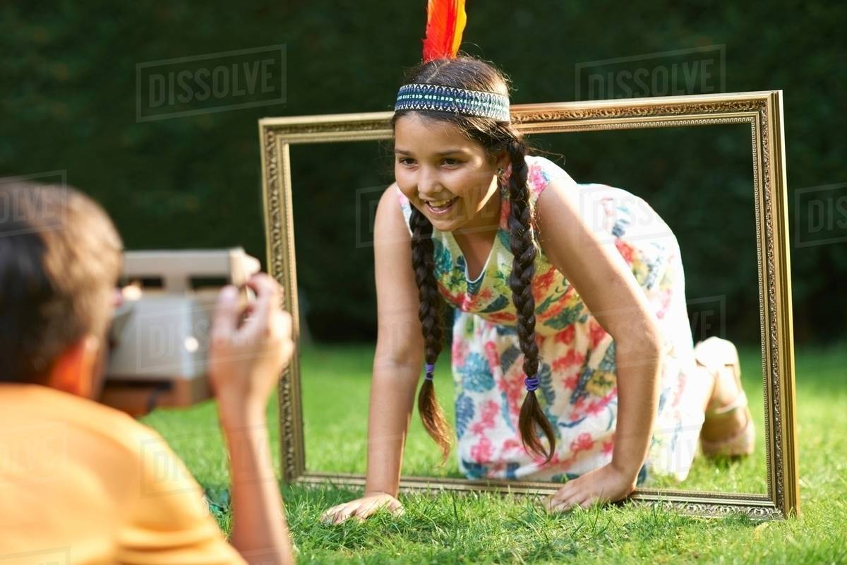 Girl kneeling, looking through picture frame, having photograph taken ...