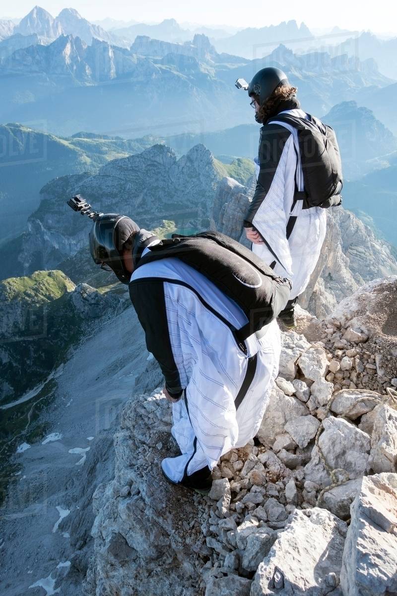 Two male BASE jumpers preparing to launch from mountain, Dolomites ...