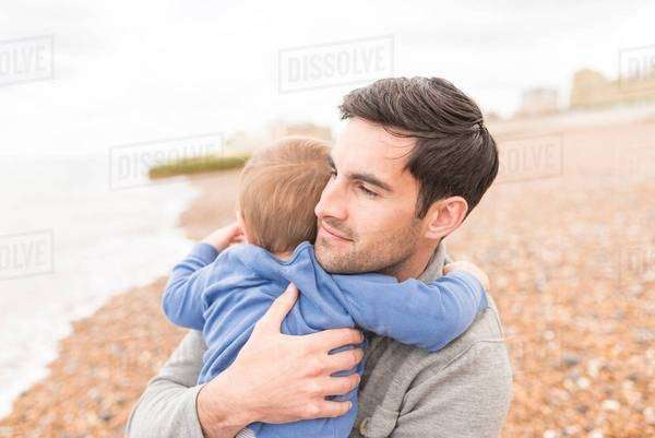 Father hugging young son on pebble beach - Stock Photo - Dissolve