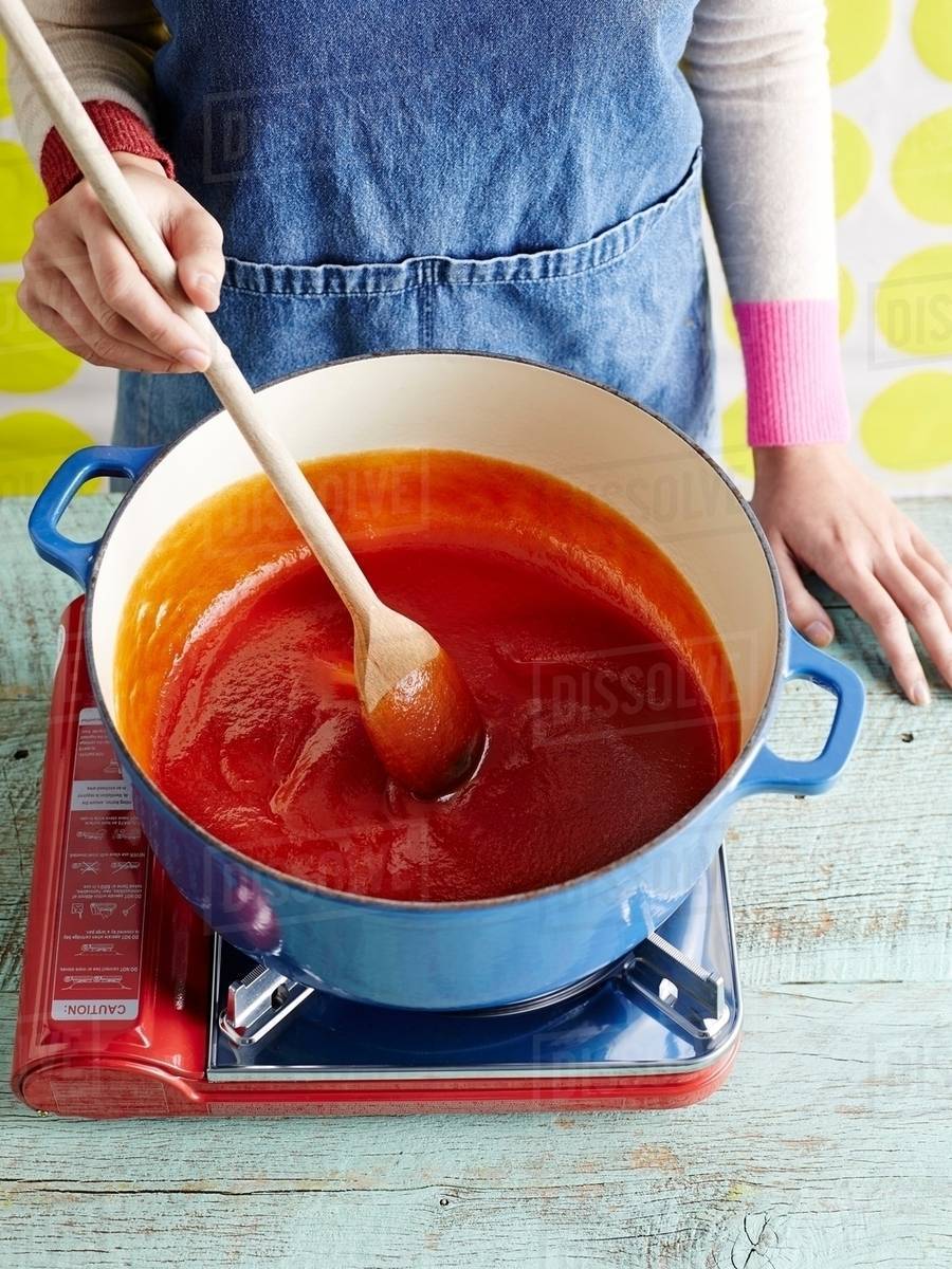 Woman preparing tomato ketchup recipe step 3, stirring pureed tomatoes ...