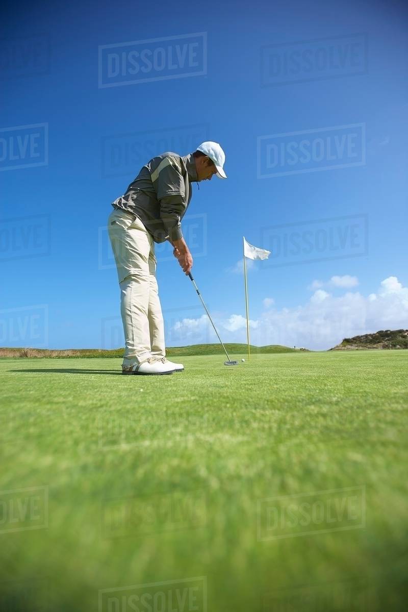 Low angle full length side view of golfer putting - Stock Photo - Dissolve