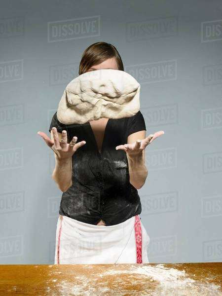 Studio portrait of young woman throwing bread dough mid air - Royalty ...