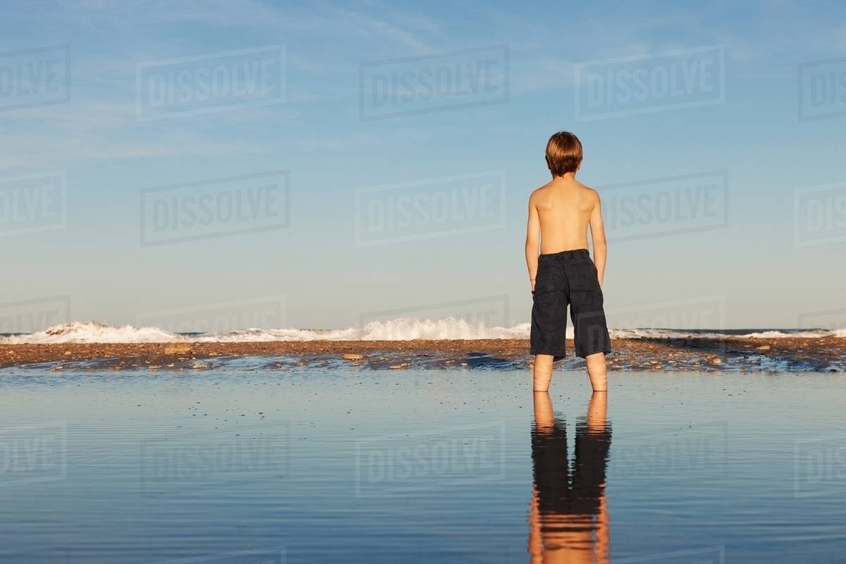 Boy and reflection standing on the beach - Stock Photo - Dissolve