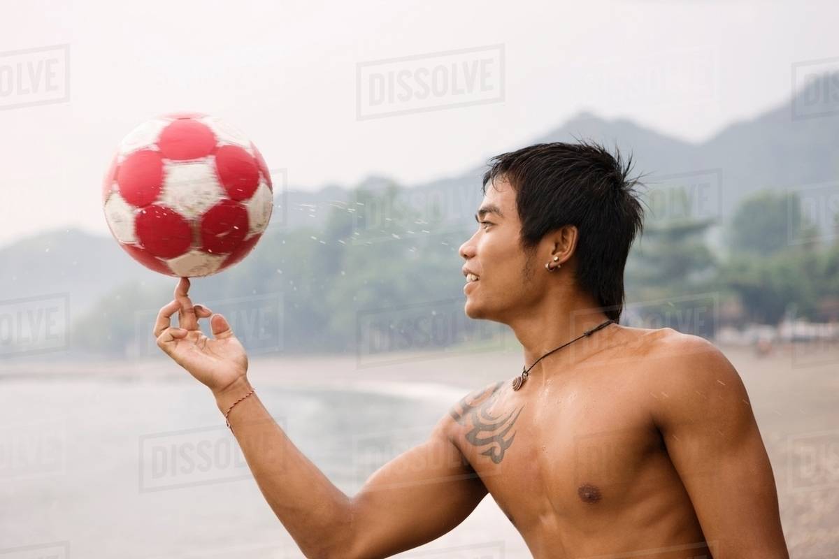 Guy spinning football on finger on beach - Royalty-free Stock Photo ...