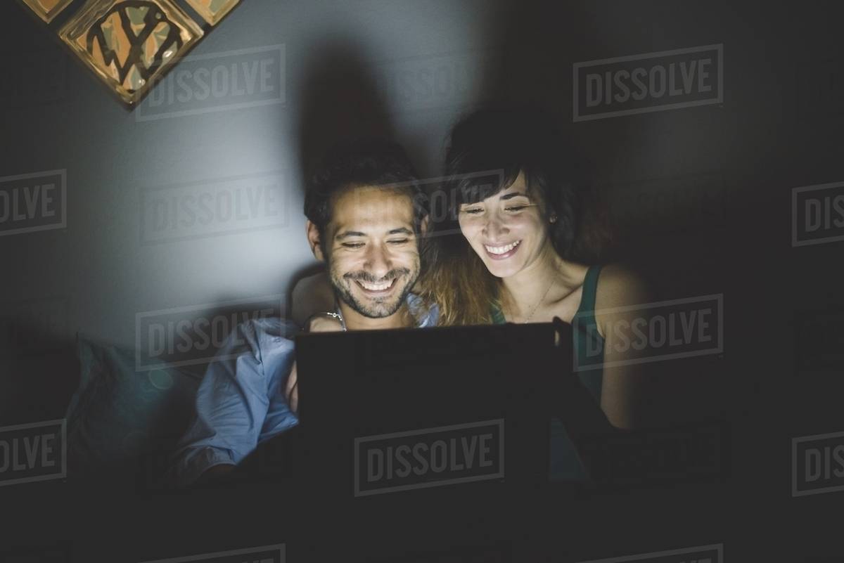 Front view of young couple illuminated by laptop computer screen ...