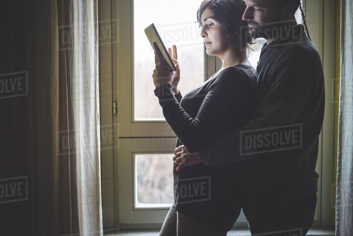 Couple standing beside window, using digital tablet - Stock Photo ...