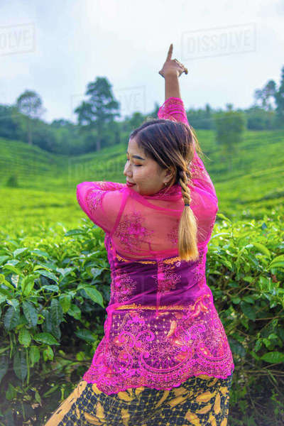 an Asian woman in a pink costume is posing in front of a tea plantation ...