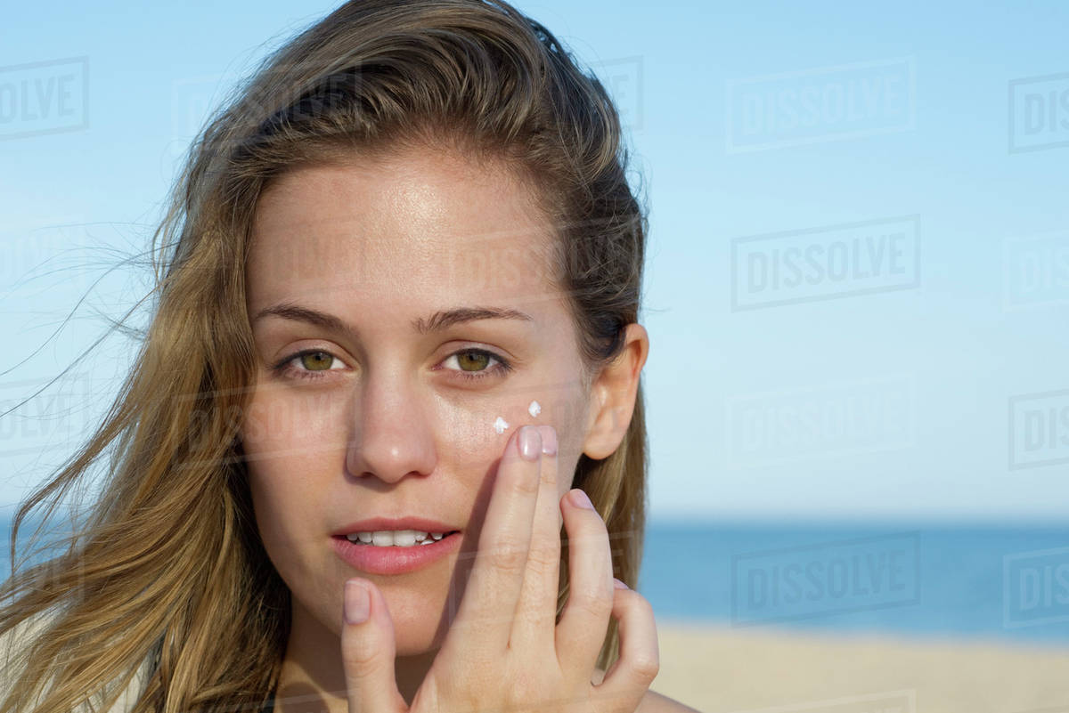 Woman applying sunscreen at the beach, portrait - Stock Photo - Dissolve