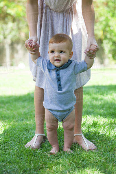 Baby standing outdoors, holding mother's hands for support - Royalty ...