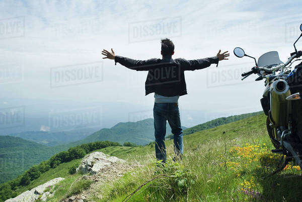Man standing by motorcycle on top of mountain, arms outstretched ...