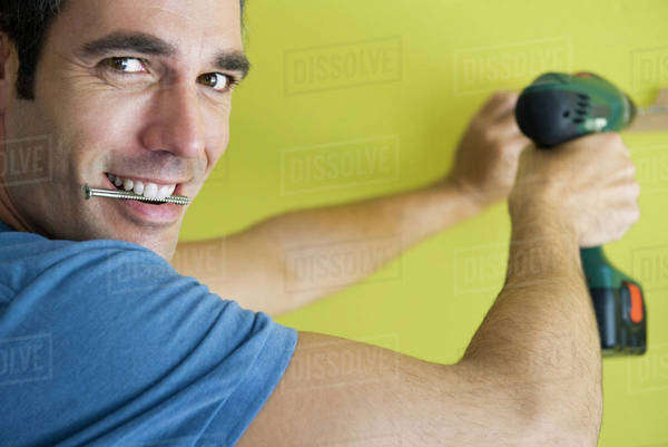 Man using power drill, biting screw in mouth - Stock Photo - Dissolve