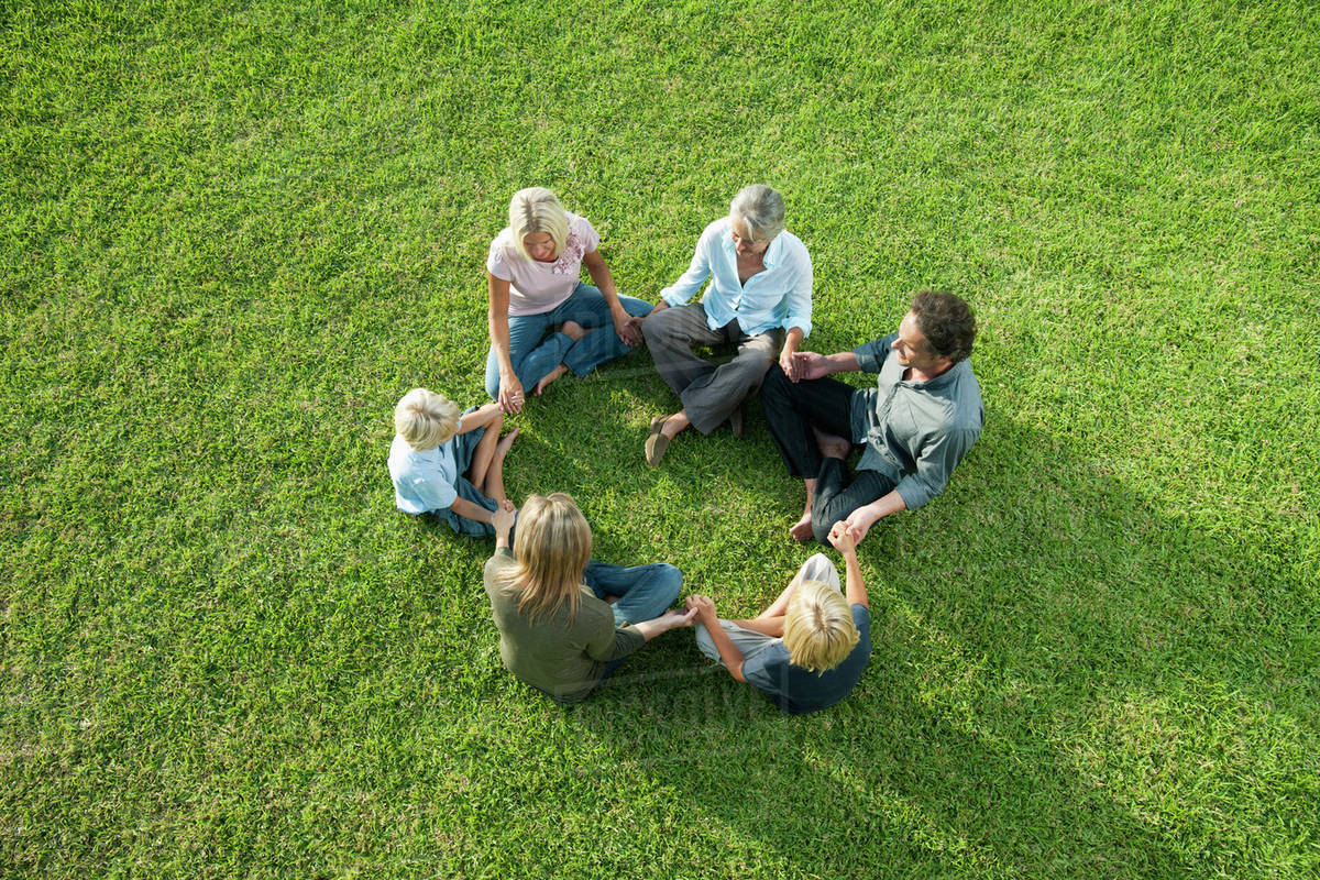 People sitting in circle on grass holding hands - Stock Photo - Dissolve