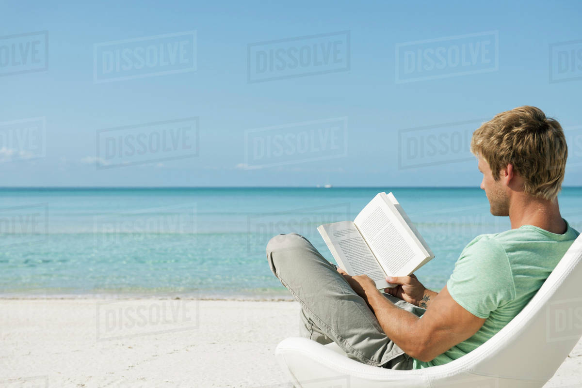 Young man reading book on beach - Stock Photo - Dissolve