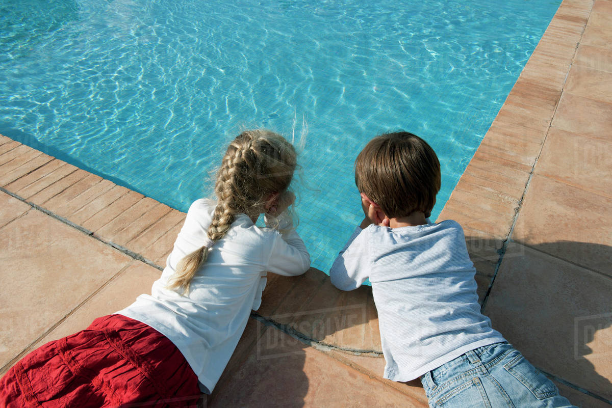 Children lying beside swimming pool, gazing at water - Royalty-free ...