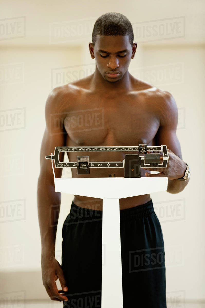 Young man standing on weight scale - Royalty-free Stock Photo | Dissolve