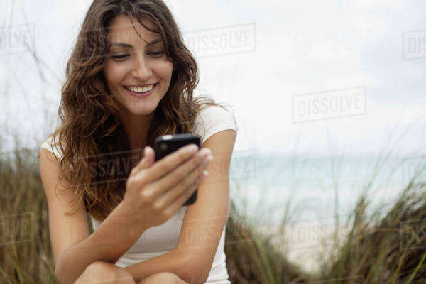 Smiling young woman looking at cell phone - Stock Photo - Dissolve