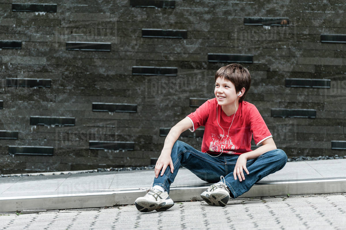 Boy sitting on sidewalk listening to music with earphones - Royalty ...