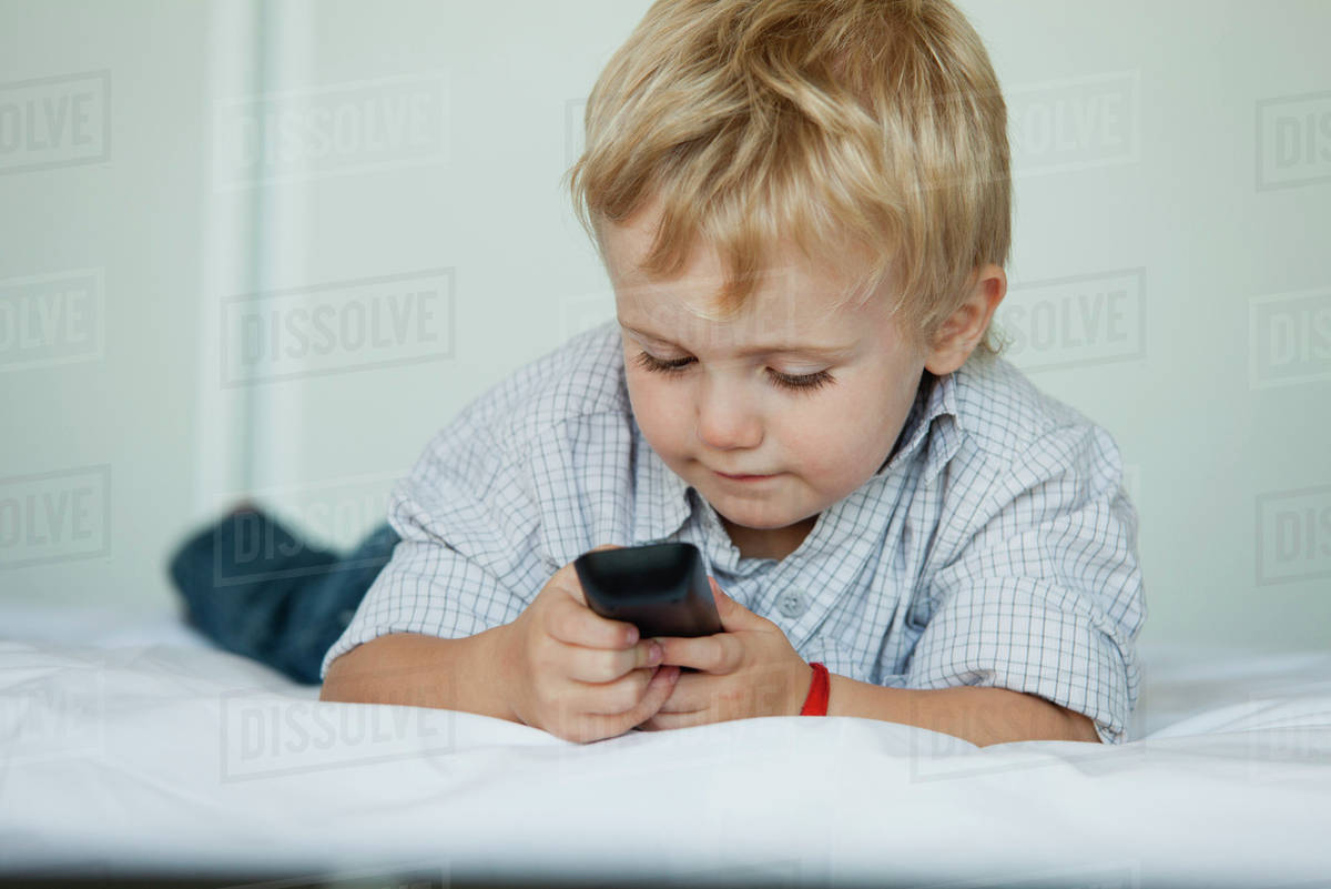Little boy lying on bed holding cell phone - Royalty-free Stock Photo ...