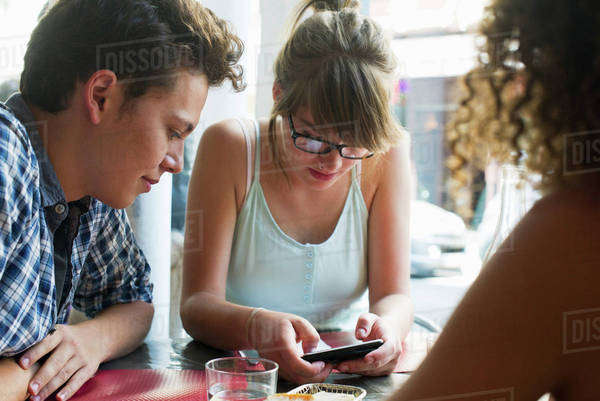 Friends hanging out in cafe, woman text messaging on cell phone ...