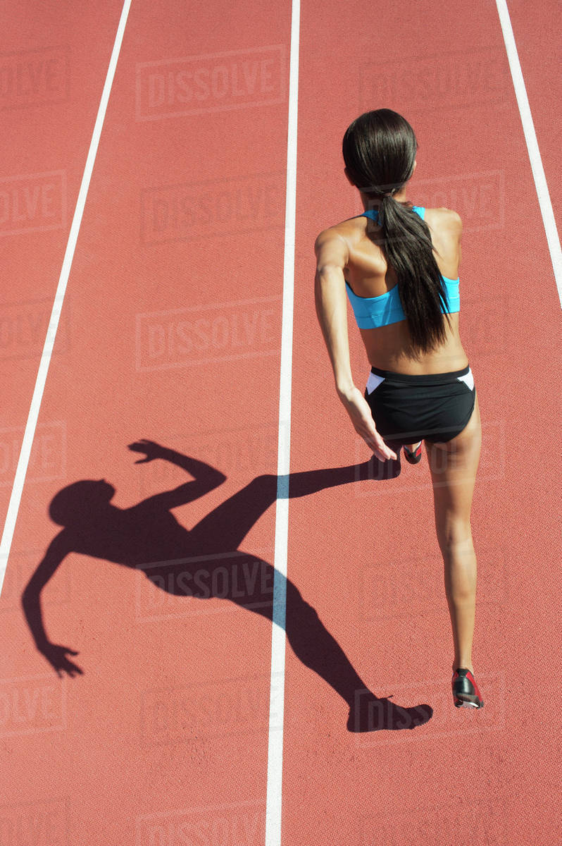 Female athlete running on track, focus on shadow - Stock Photo - Dissolve