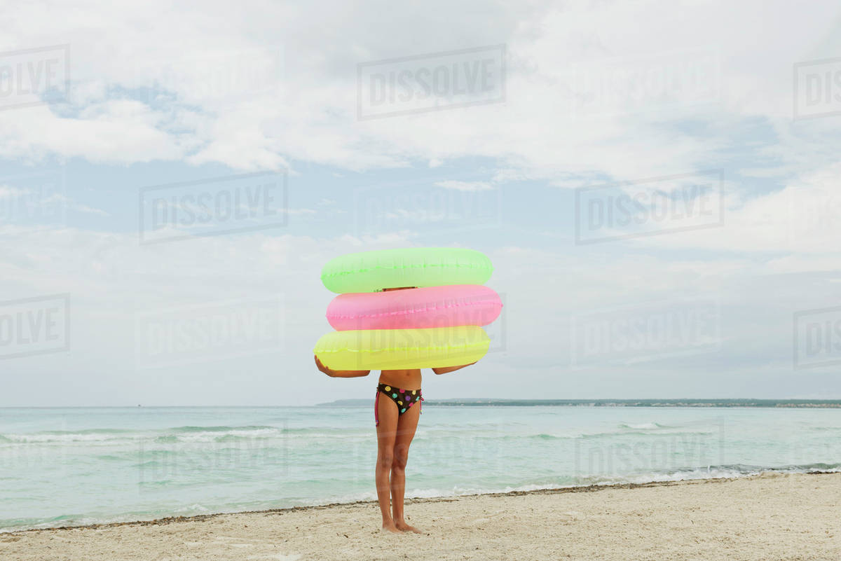 Girl holding stack of inflatable rings on beach, face obscured ...