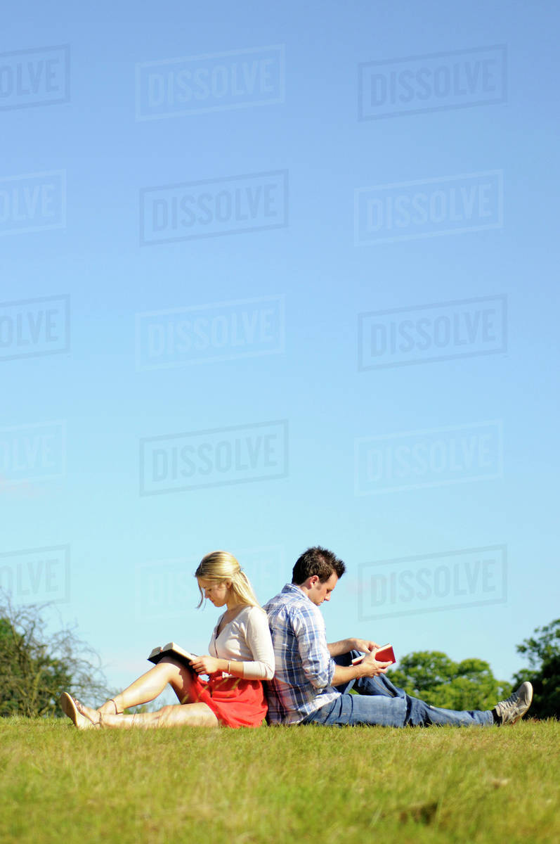Couple sitting back to back reading in park - Royalty-free Stock Photo ...