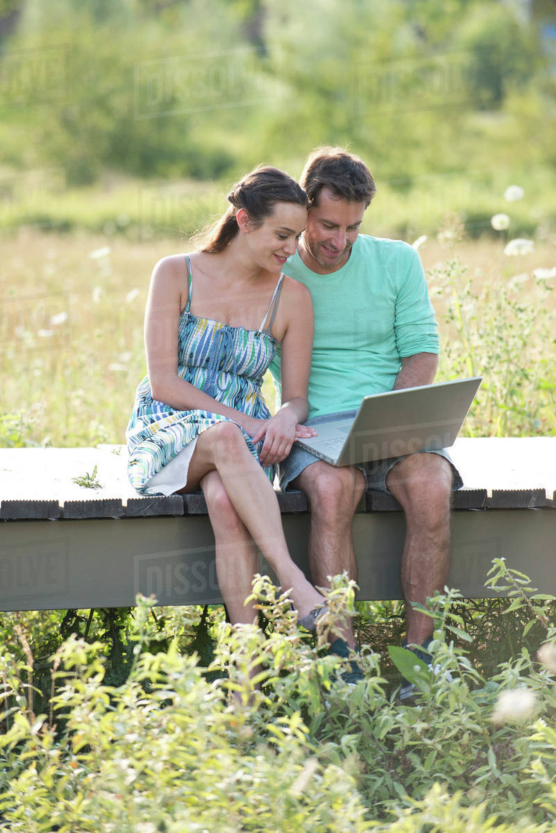 Couple sitting on countryside boardwalk using laptop computer - Royalty ...