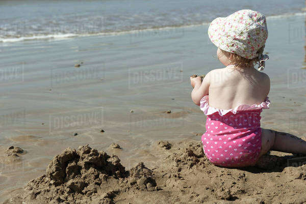 Toddler girl playing in sand at the beach, rear view - Royalty-free ...