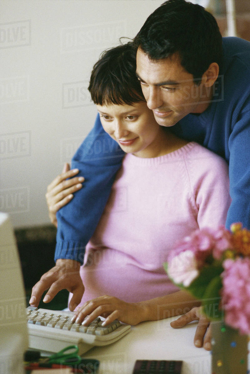 Couple typing on keyboard together, man leaning over woman's shoulder ...
