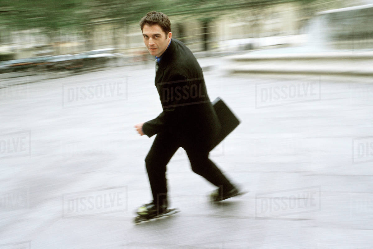Man in business attire inline skating carrying briefcase in city square ...