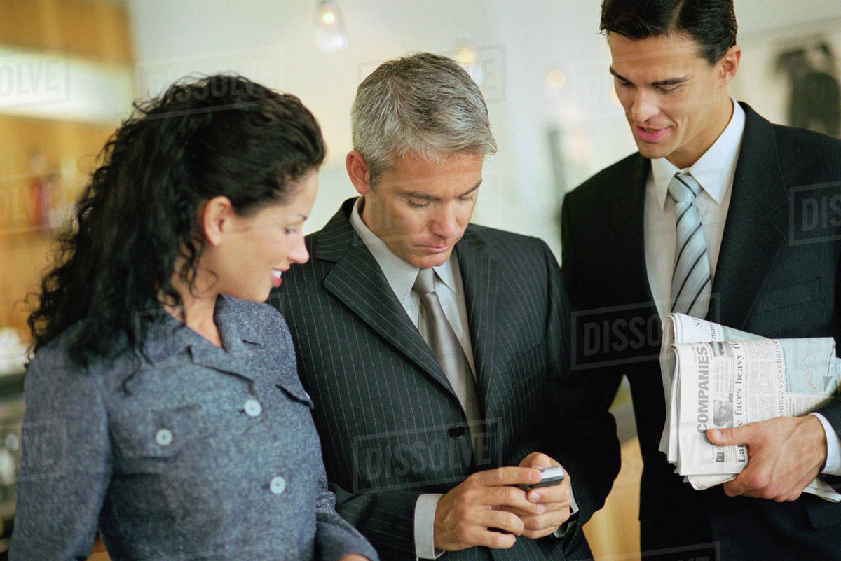 Business associates standing together, looking at cell phone - Royalty ...