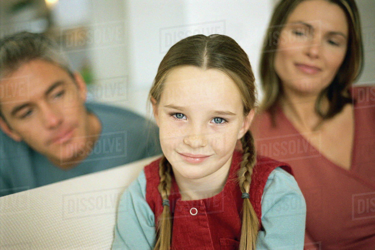 Little girl smiling at camera, parents in background - Stock Photo ...