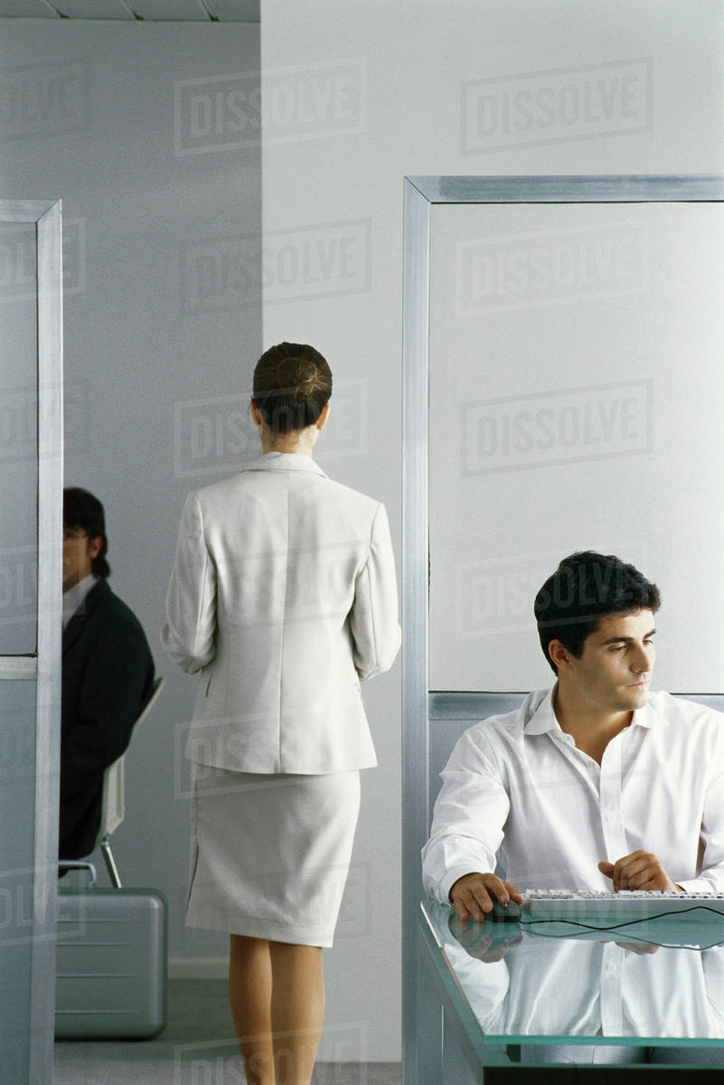 Female executive walking through office while colleagues work, rear ...