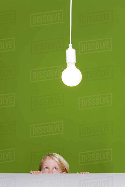 Little girl looking fearfully up at illuminated light bulb suspended ...