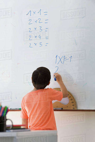 Elementary school student doing math equation on whiteboard, rear view ...