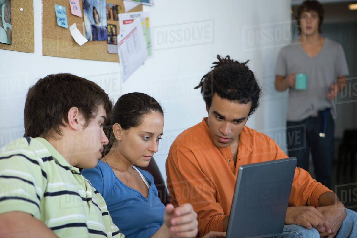 Female college student using laptop computer, friends sitting on either ...