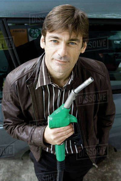 Man at gas station holding gas nozzle - Stock Photo - Dissolve