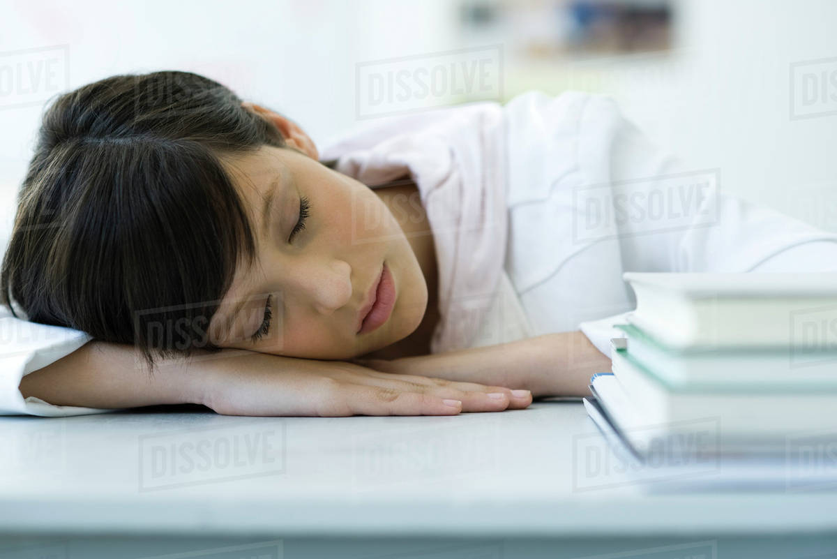 High school student napping with head on desk, stack of books in ...