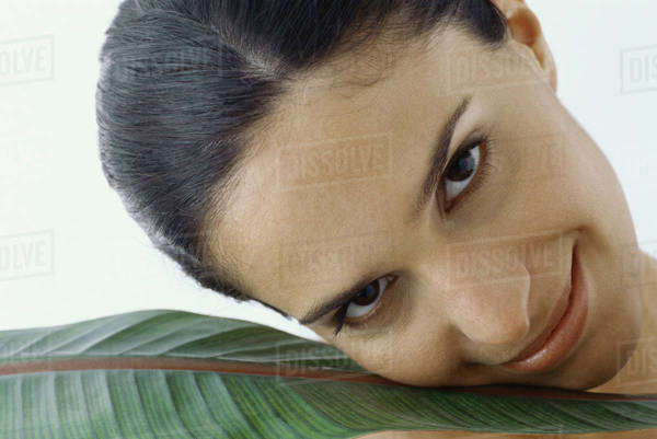 Young woman resting cheek on large tropical leaf, smiling, portrait ...