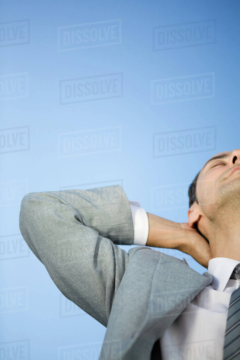 Businessman leaning back, hands behind head, eyes closed, cropped view ...